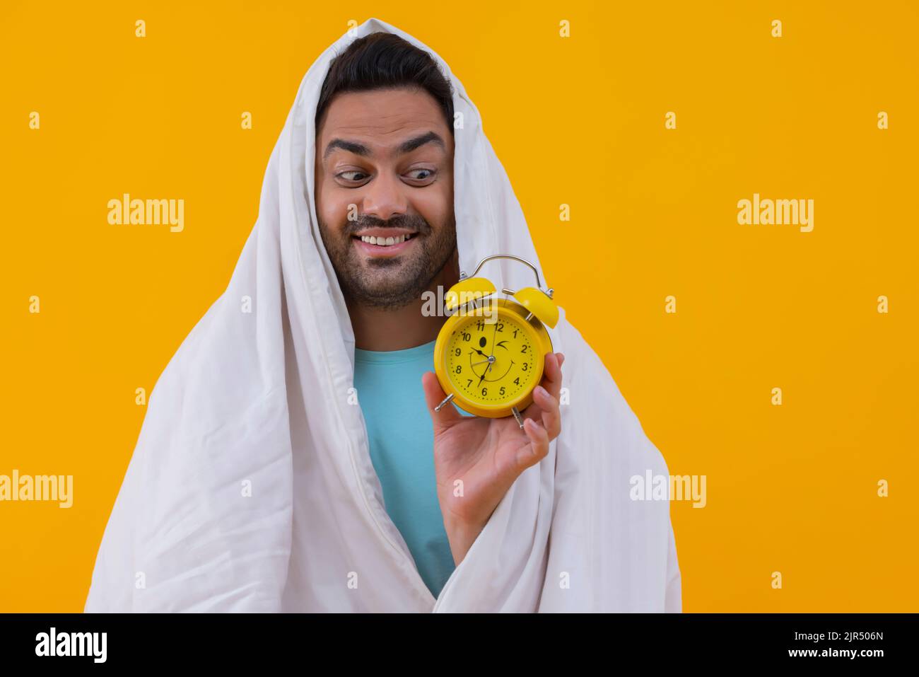 Portrait of a cheerful young man holding alarm clock over yellow ...