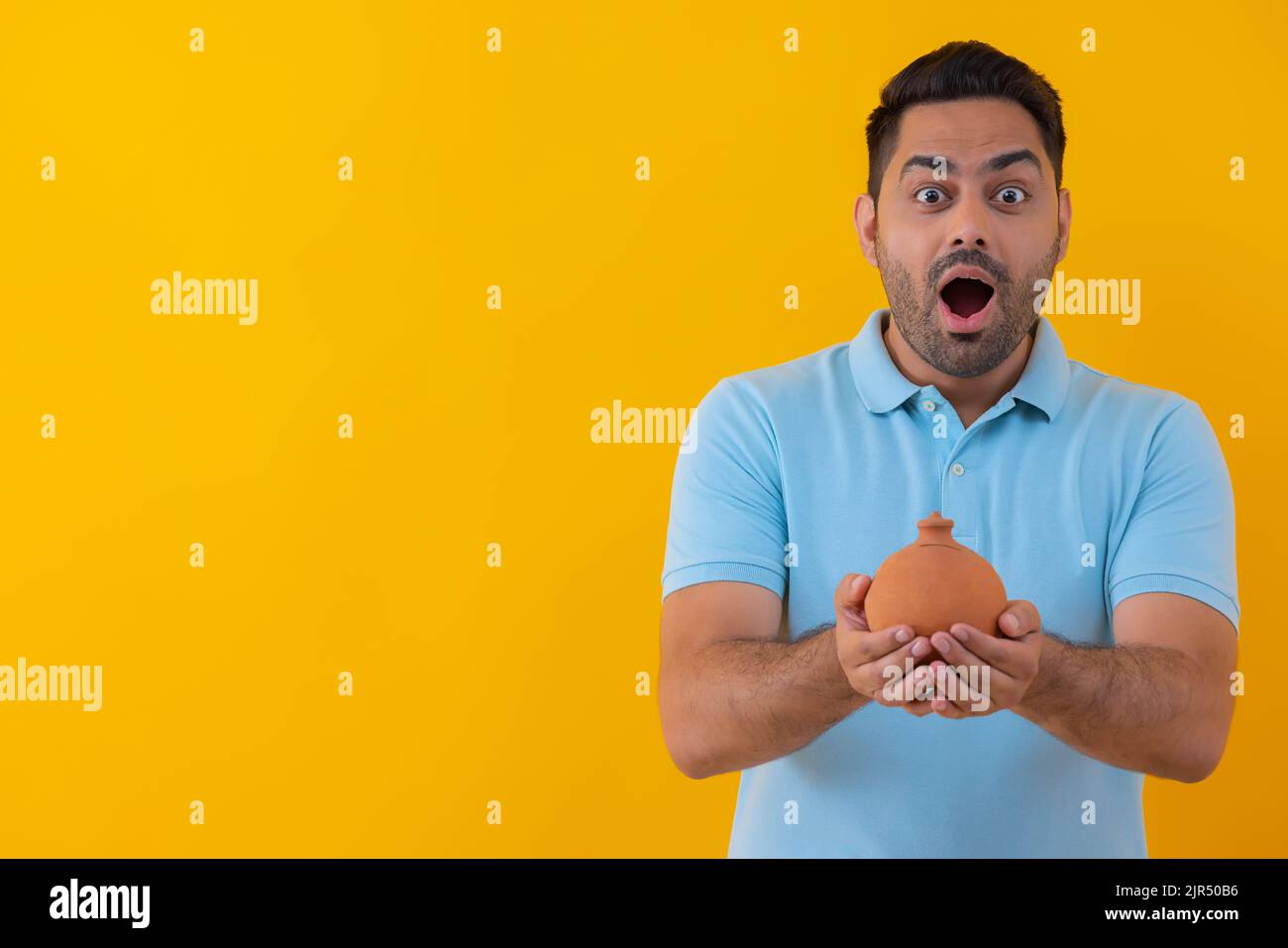 Portrait of a surprised young man standing with a clay saving pot in ...