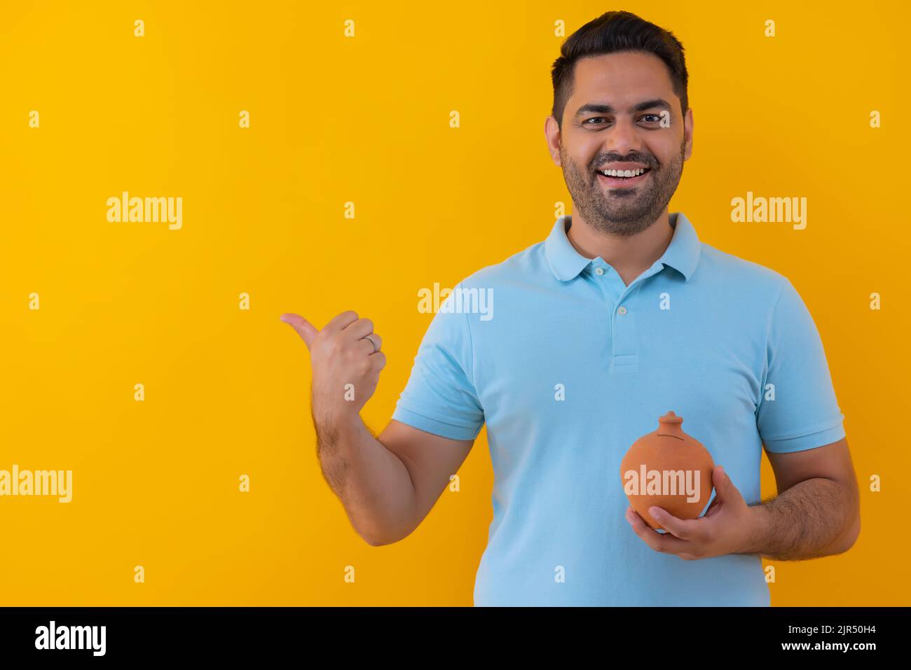 Cheerful young man pointing sideways with a clay saving pot in his hand ...
