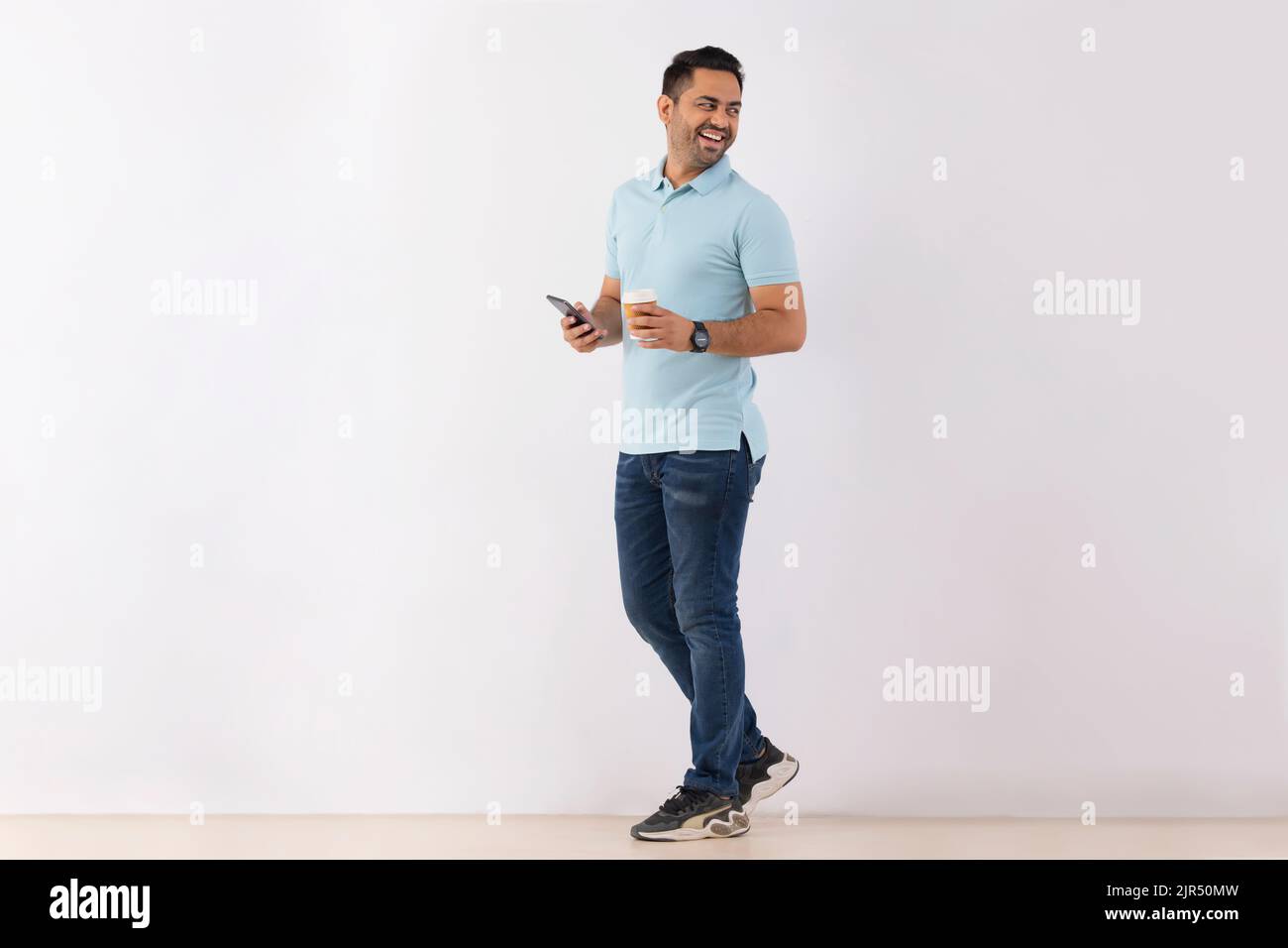 Cheerful young man looking back while standing with Smartphone and ...
