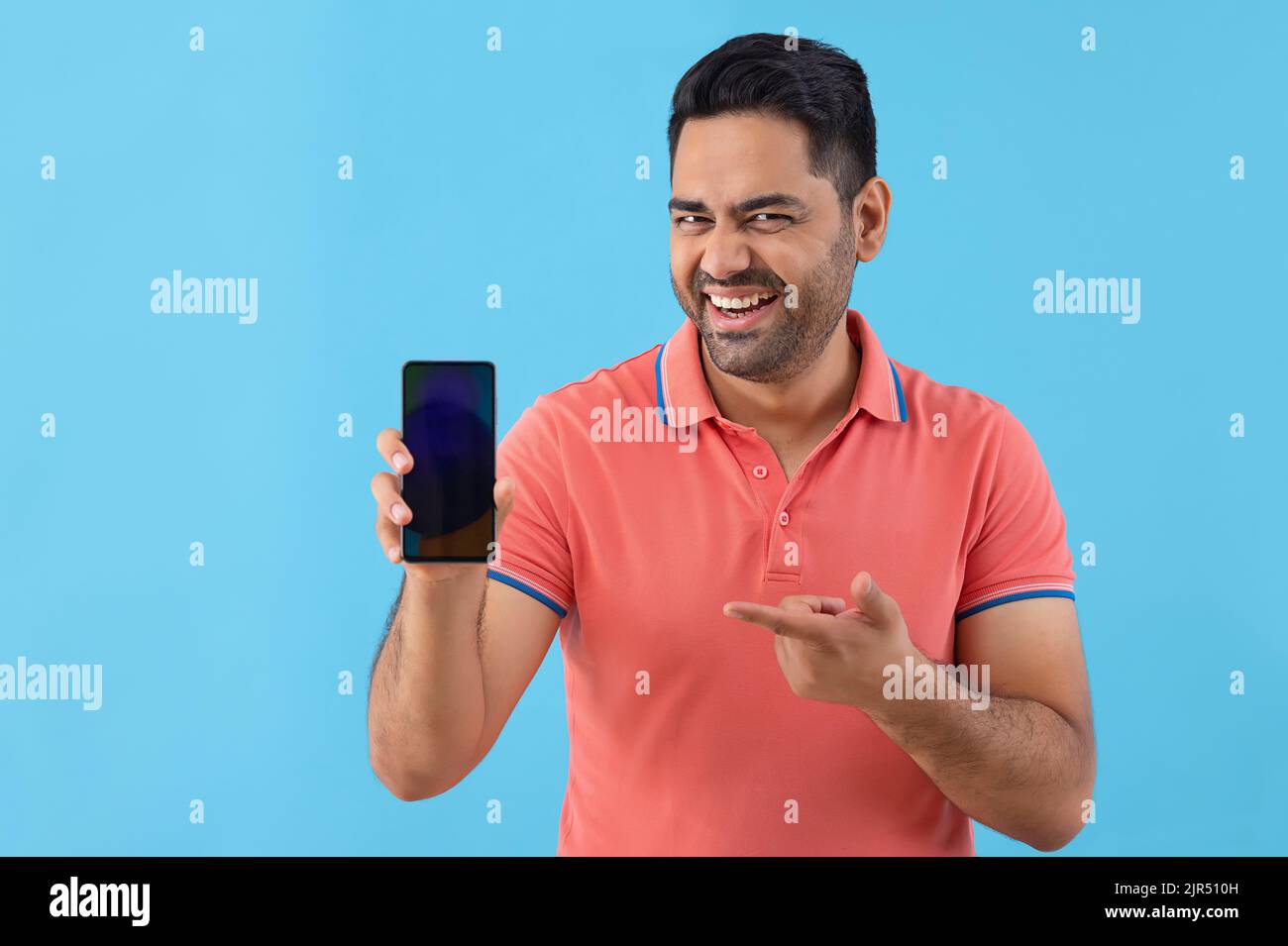 Cheerful young man looking at camera and pointing at Smartphone holding ...