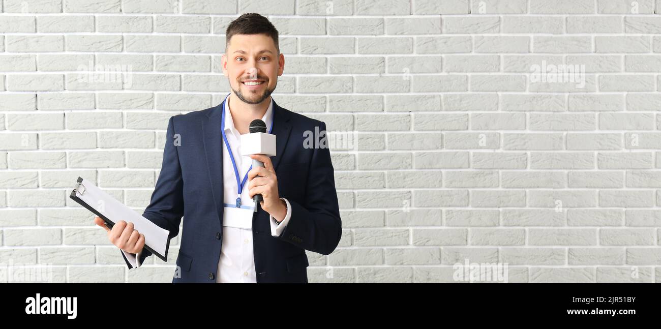 Male journalist with microphone on brick background Stock Photo - Alamy