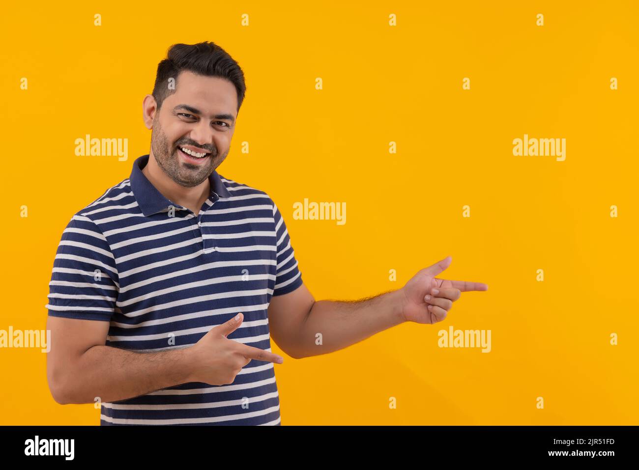 Smiling young man pointing sideways against yellow background Stock ...
