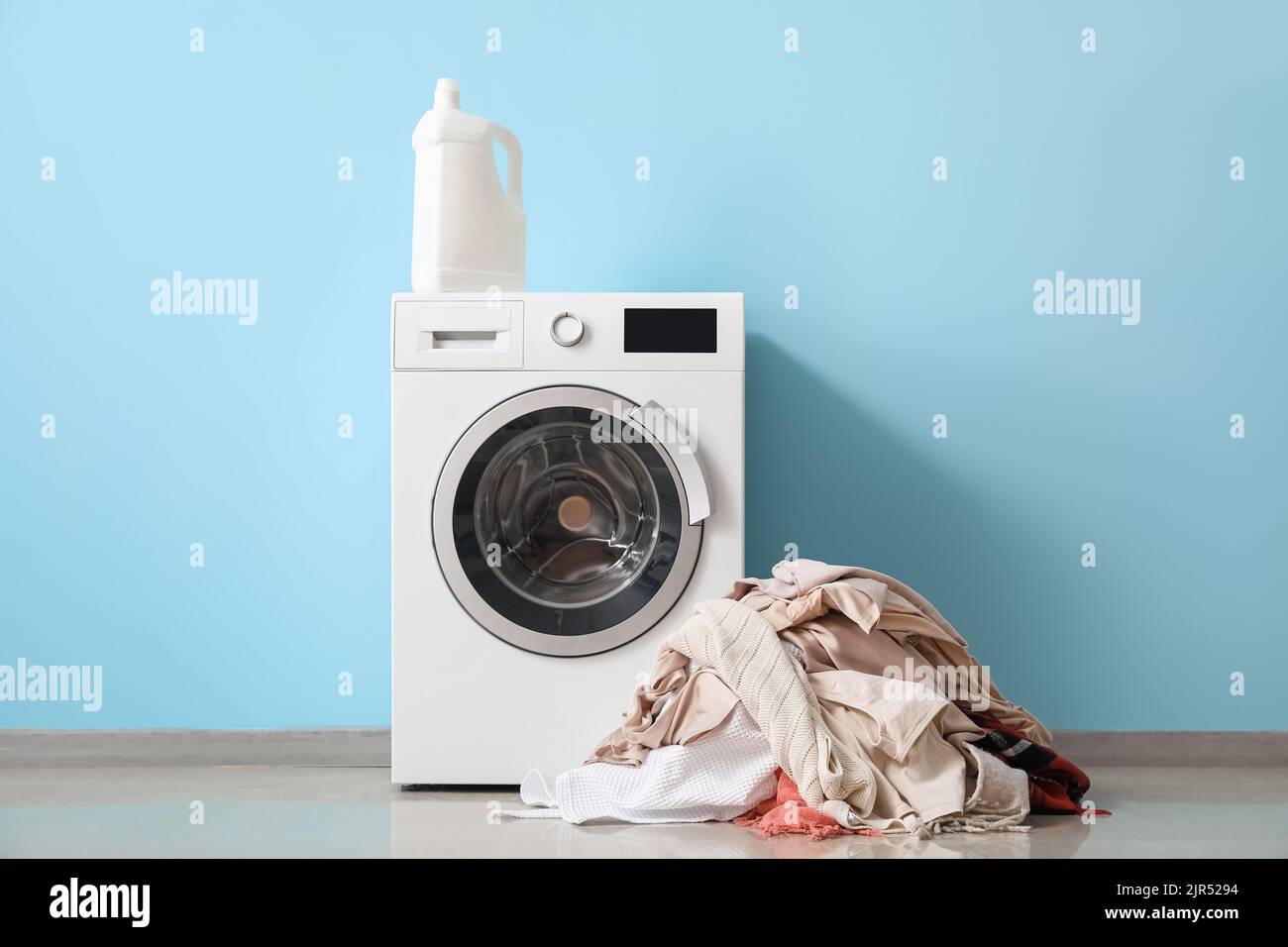 Stack of clothes and washing machine with detergent near blue wall ...