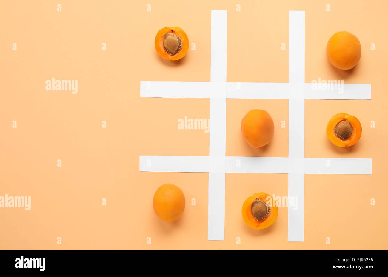 Tic tac toe game with ripe apricots and paper grid on color background ...