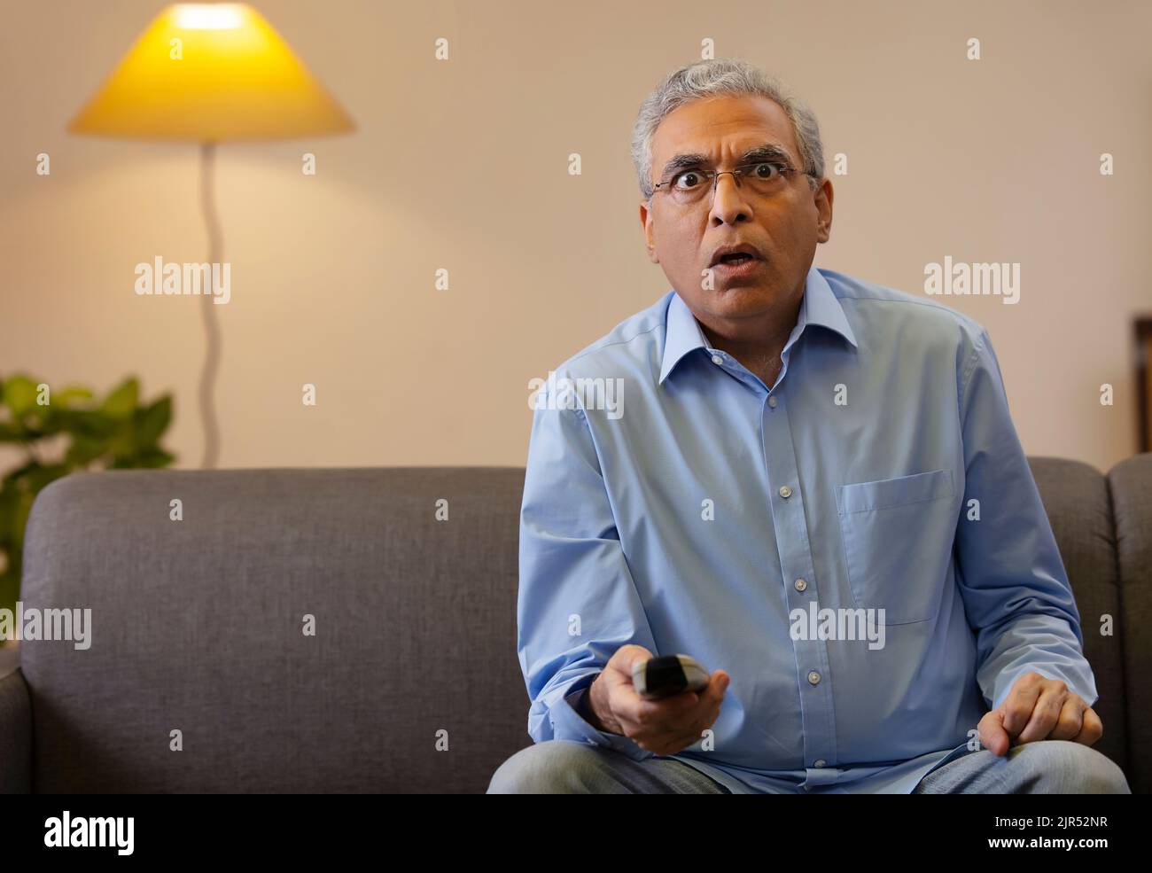 Shocked senior man sitting on sofa in the living room and watching ...