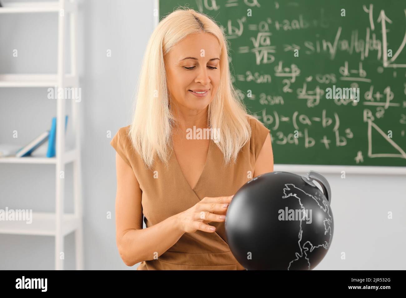 Mature Geography teacher with globe in classroom Stock Photo - Alamy
