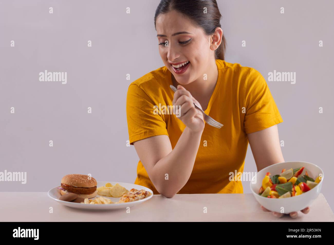 Young woman choosing between healthy and unhealthy food Stock Photo - Alamy