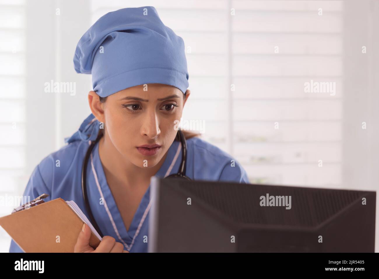 Close-up of female nurse holding clipboard and using computer in ...
