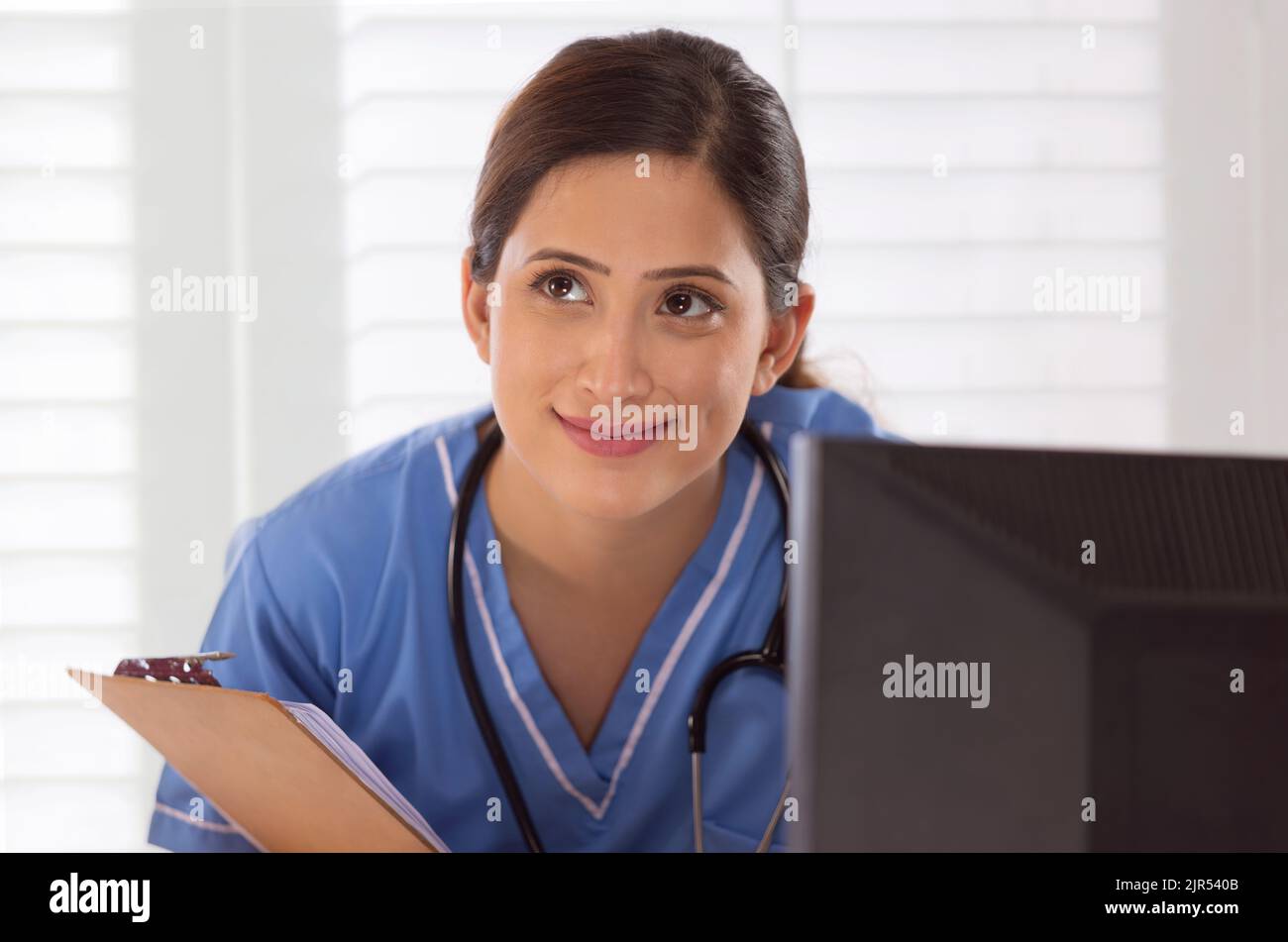 Close-up of female nurse holding clipboard and using computer in ...