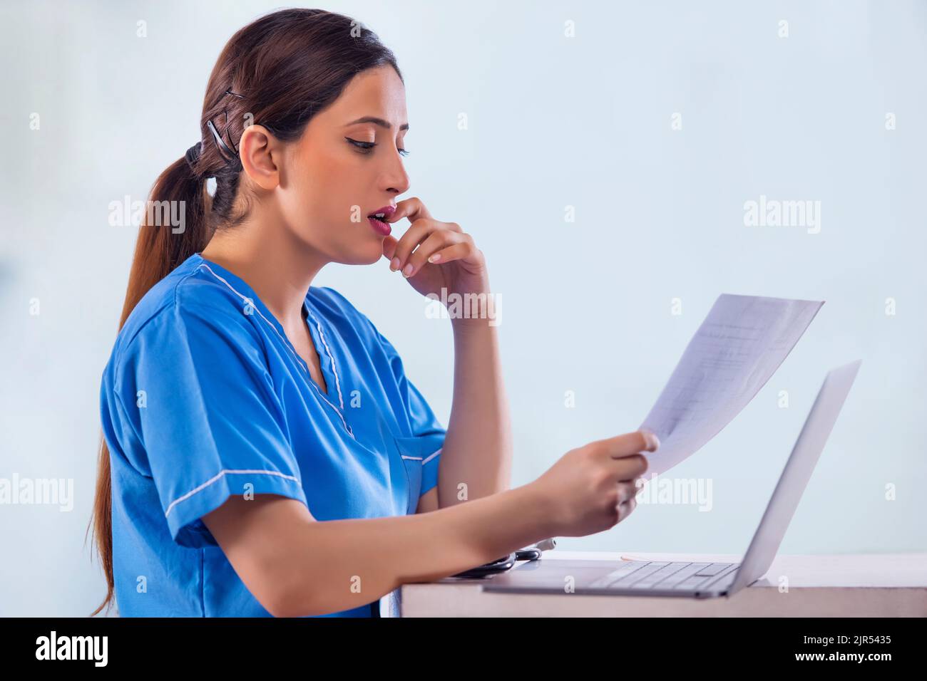 Female nurse examining document while working on laptop Stock Photo - Alamy