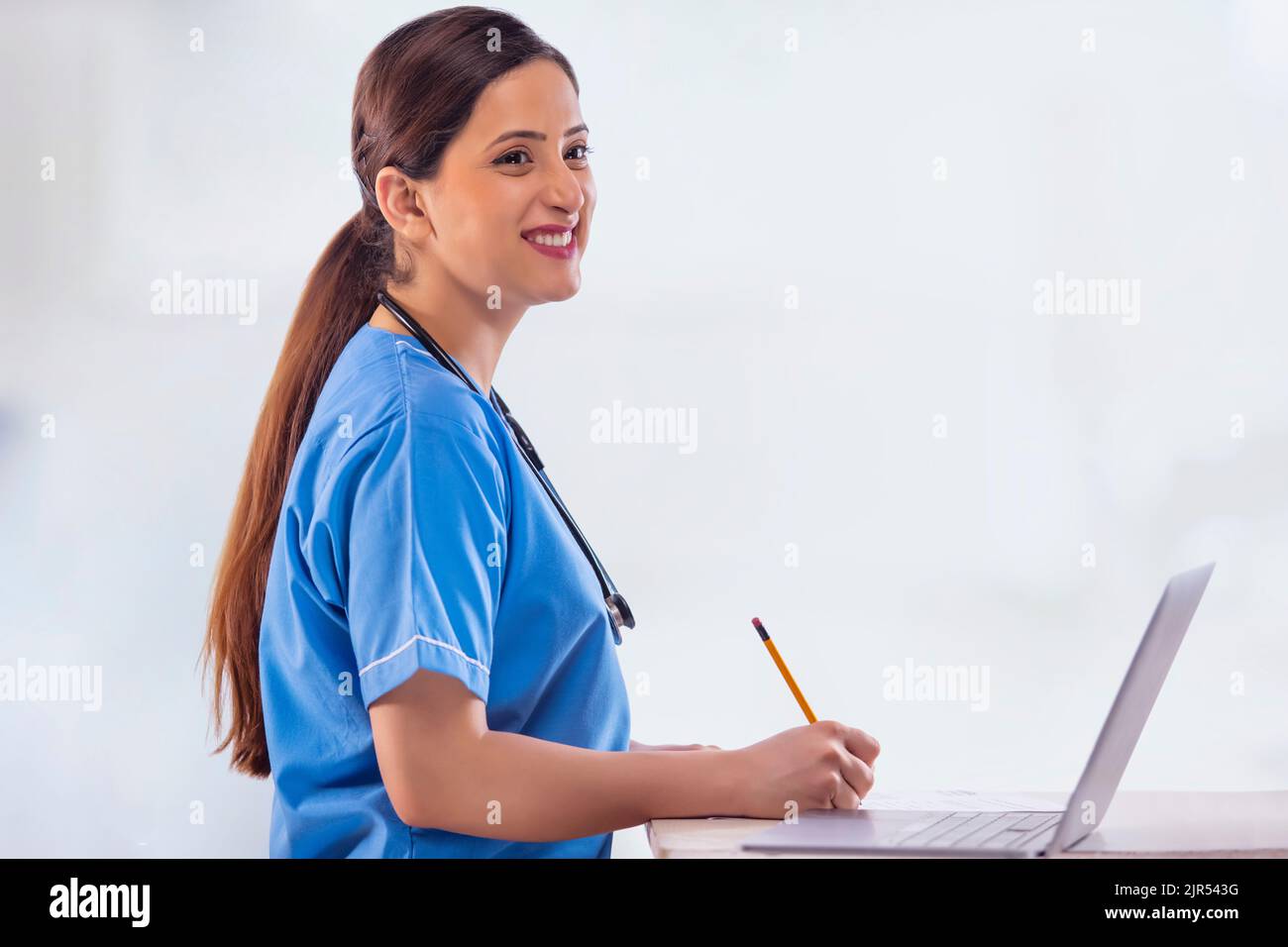 Portrait of a cheerful female nurse in blue scrub taking notes and ...