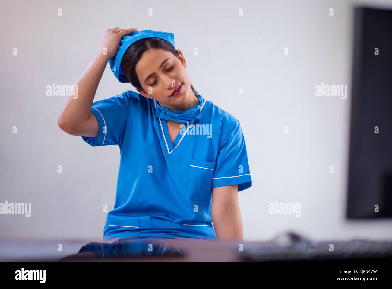 Portrait of a tired female nurse removing surgical cap while sitting at ...