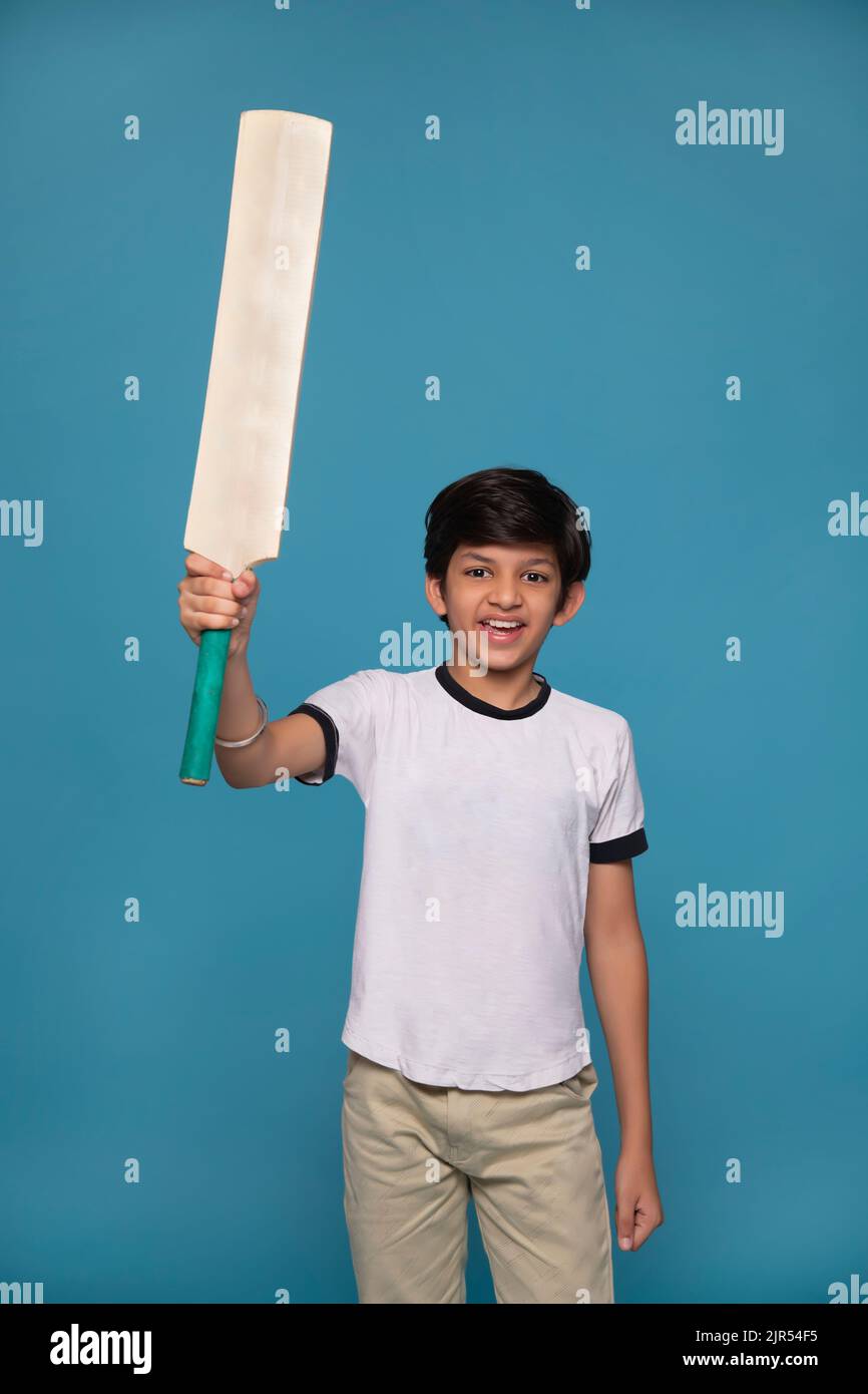 Portrait of cheerful boy showing his cricket bat against blue ...