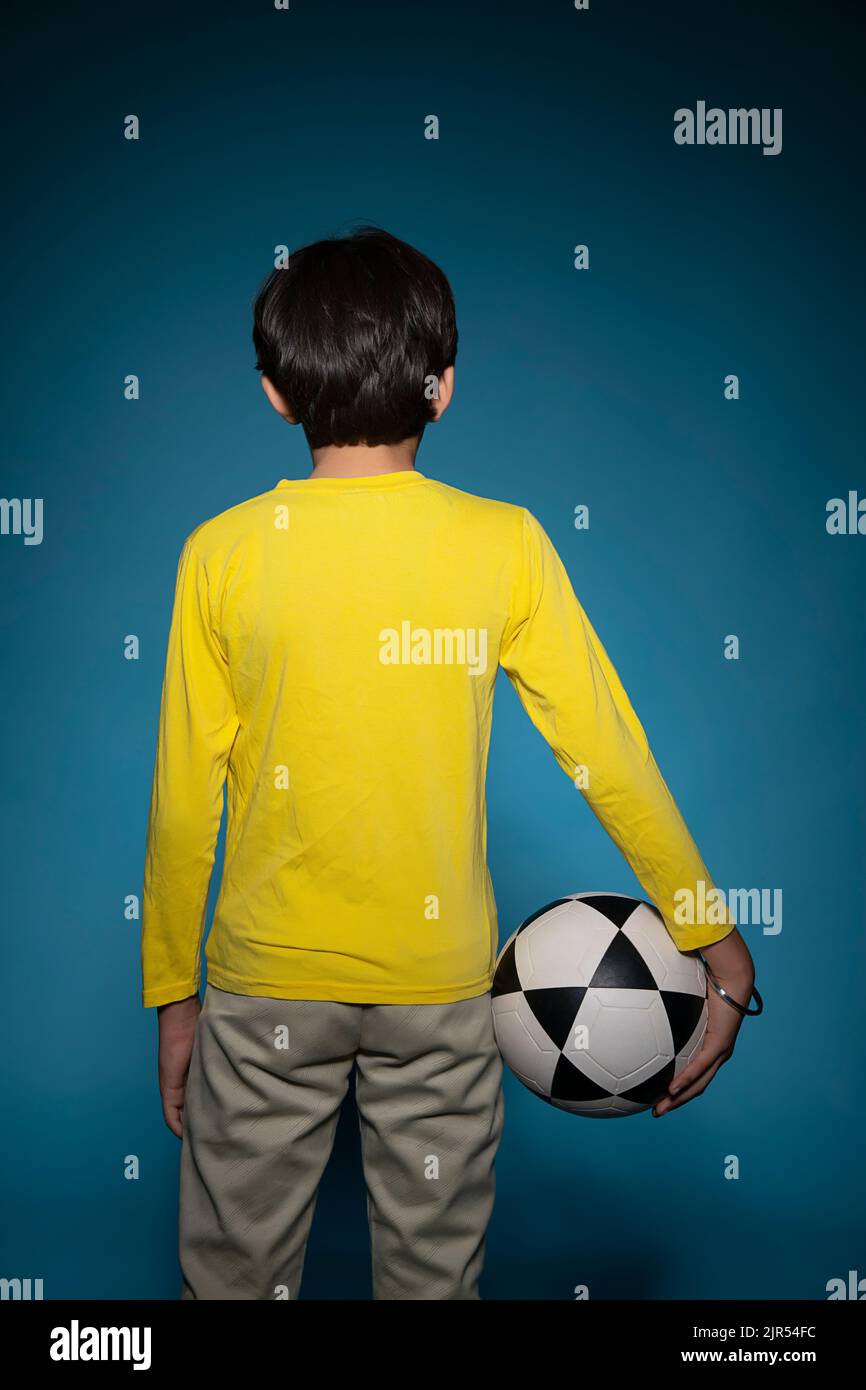 Back view of boy holding football against blue background Stock Photo ...