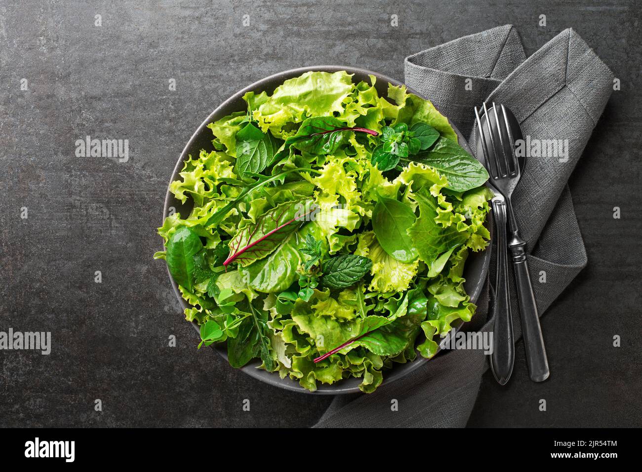 Fresh green leafy salad with herbs on dark table background. Concept ...