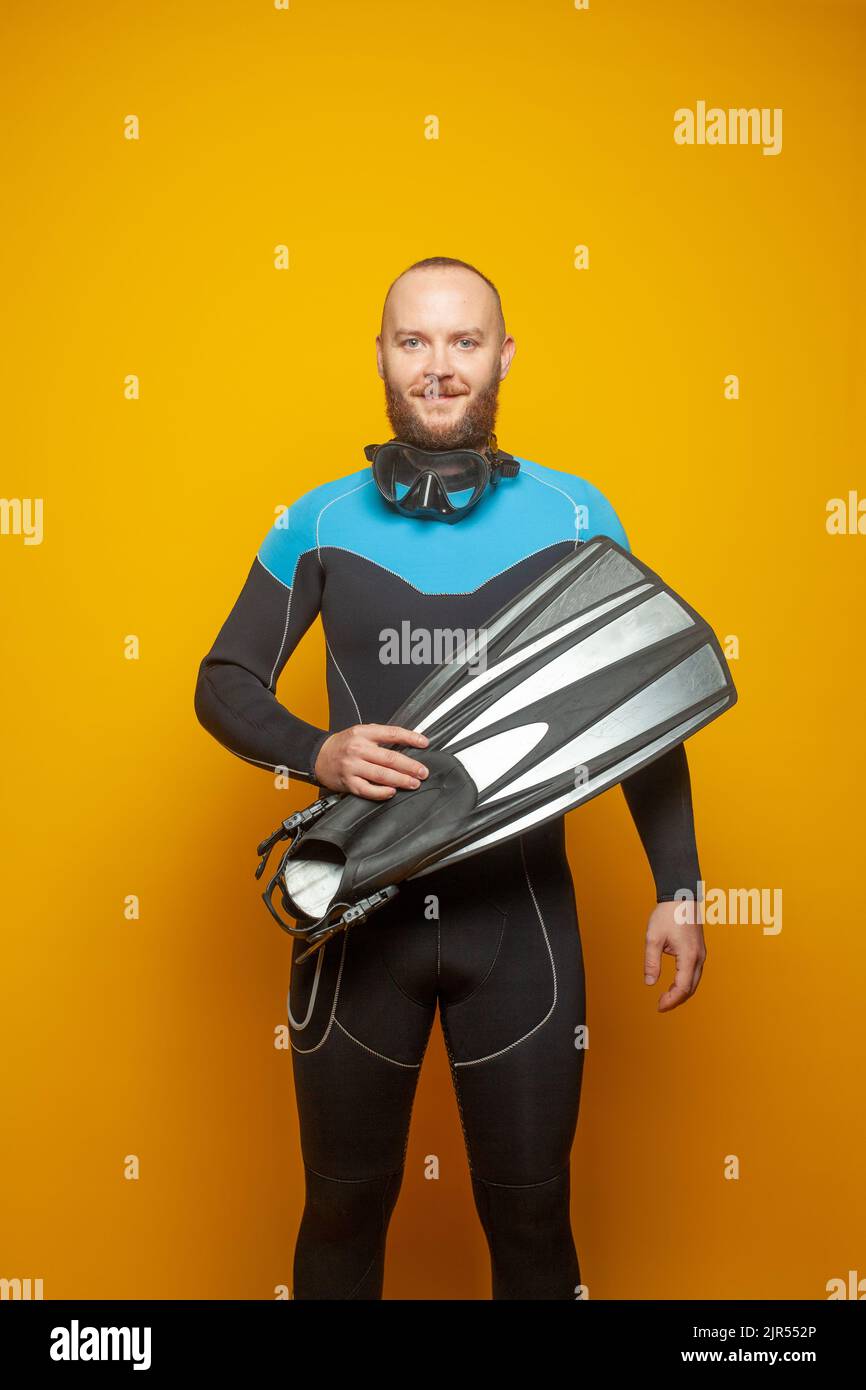 Smiling man diver standing holding fins on bright yellow studio ...