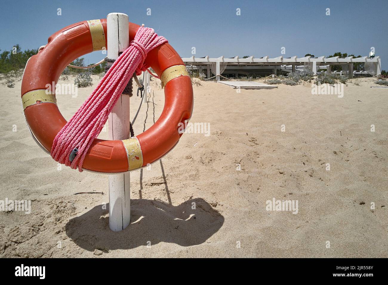 Symbolic image of a life buoy with rope hanging on a pole in the beach ...