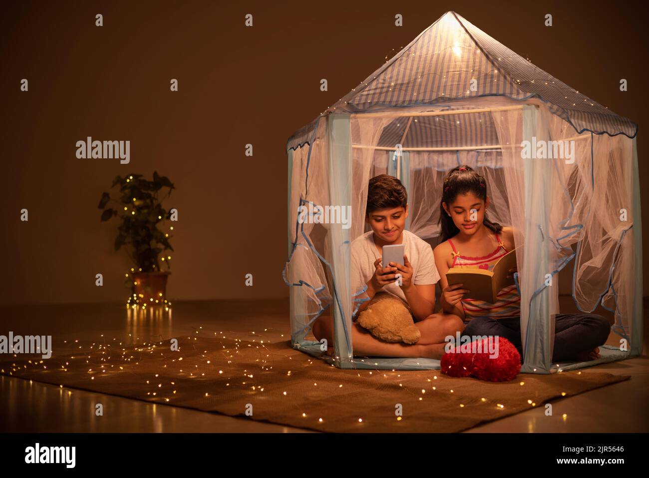 Boy using Smartphone and girl reading a book while sitting inside a ...