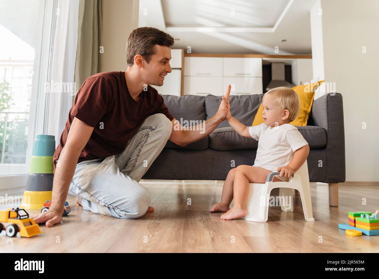 Potty training. Young father assisting his little baby boy using pot in ...