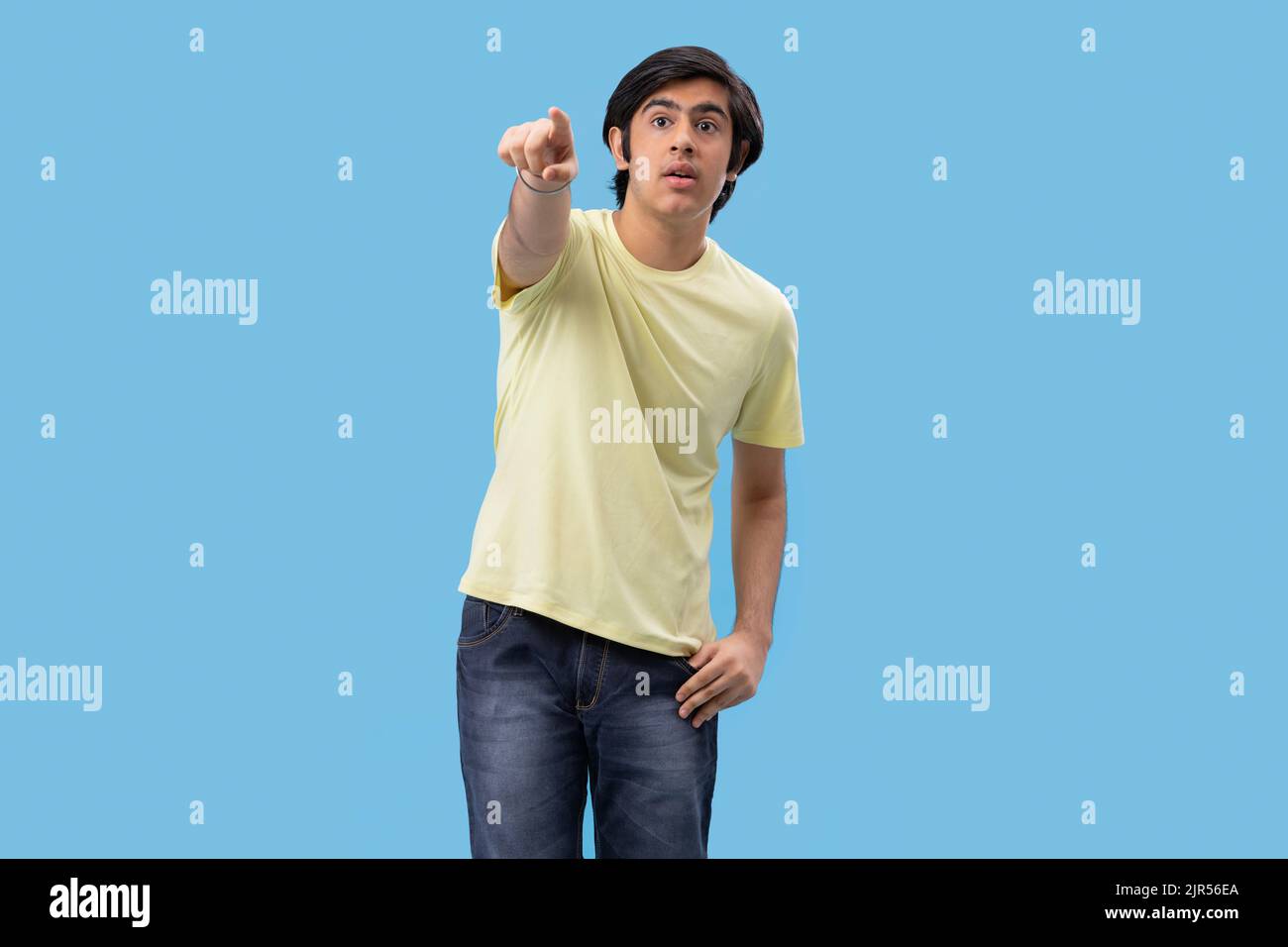 Portrait of a teenage boy pointing away while standing against blue ...