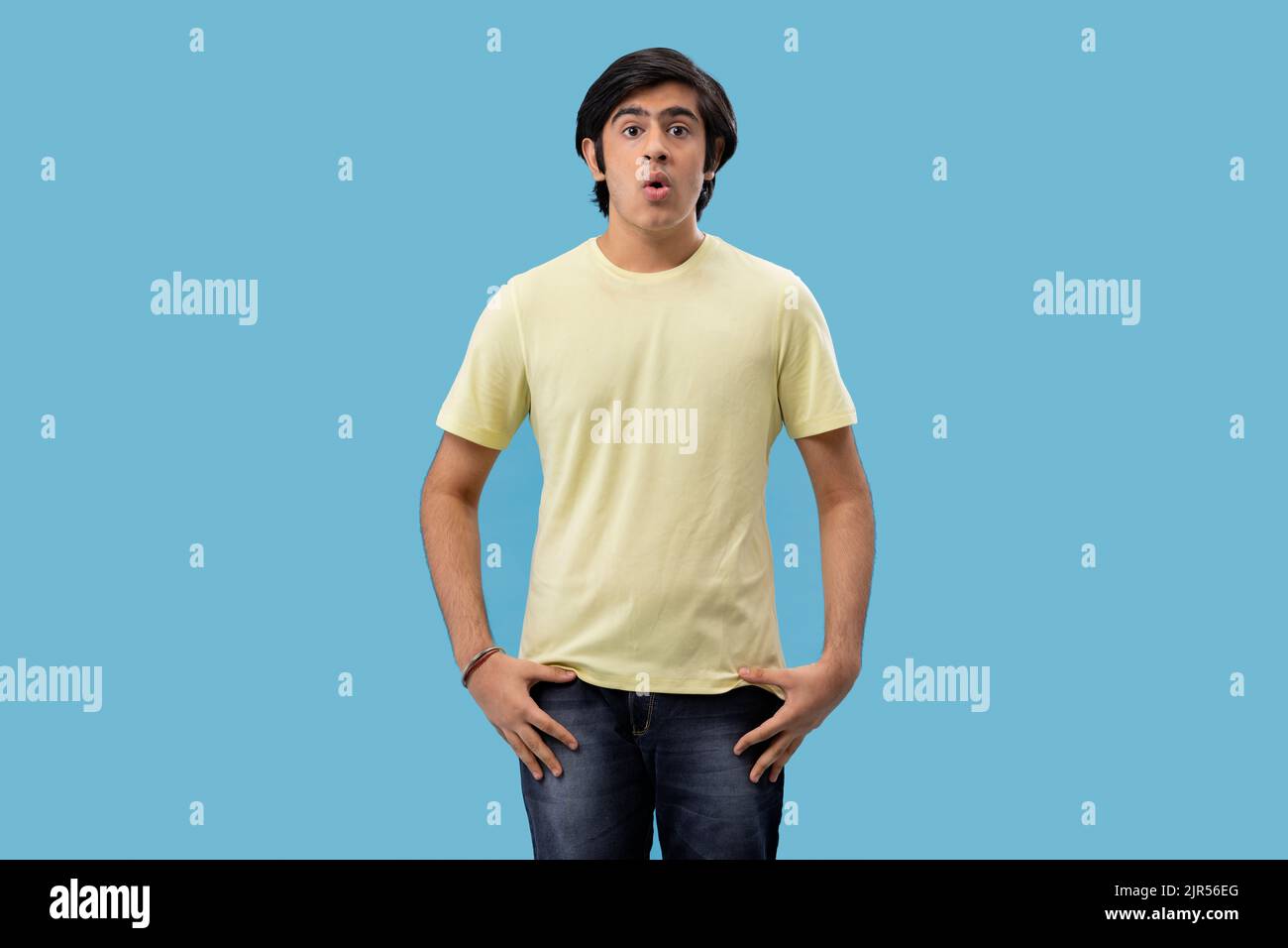 Portrait of a shocked teenage boy gesturing while standing against blue background Stock Photo ...