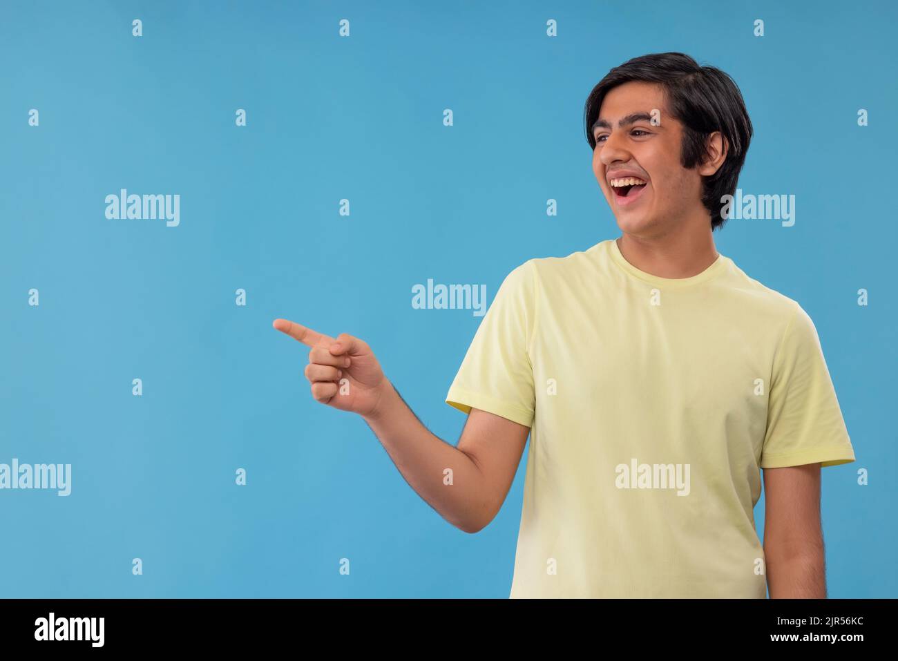 Portrait of a teenage boy pointing sideways against blue background ...