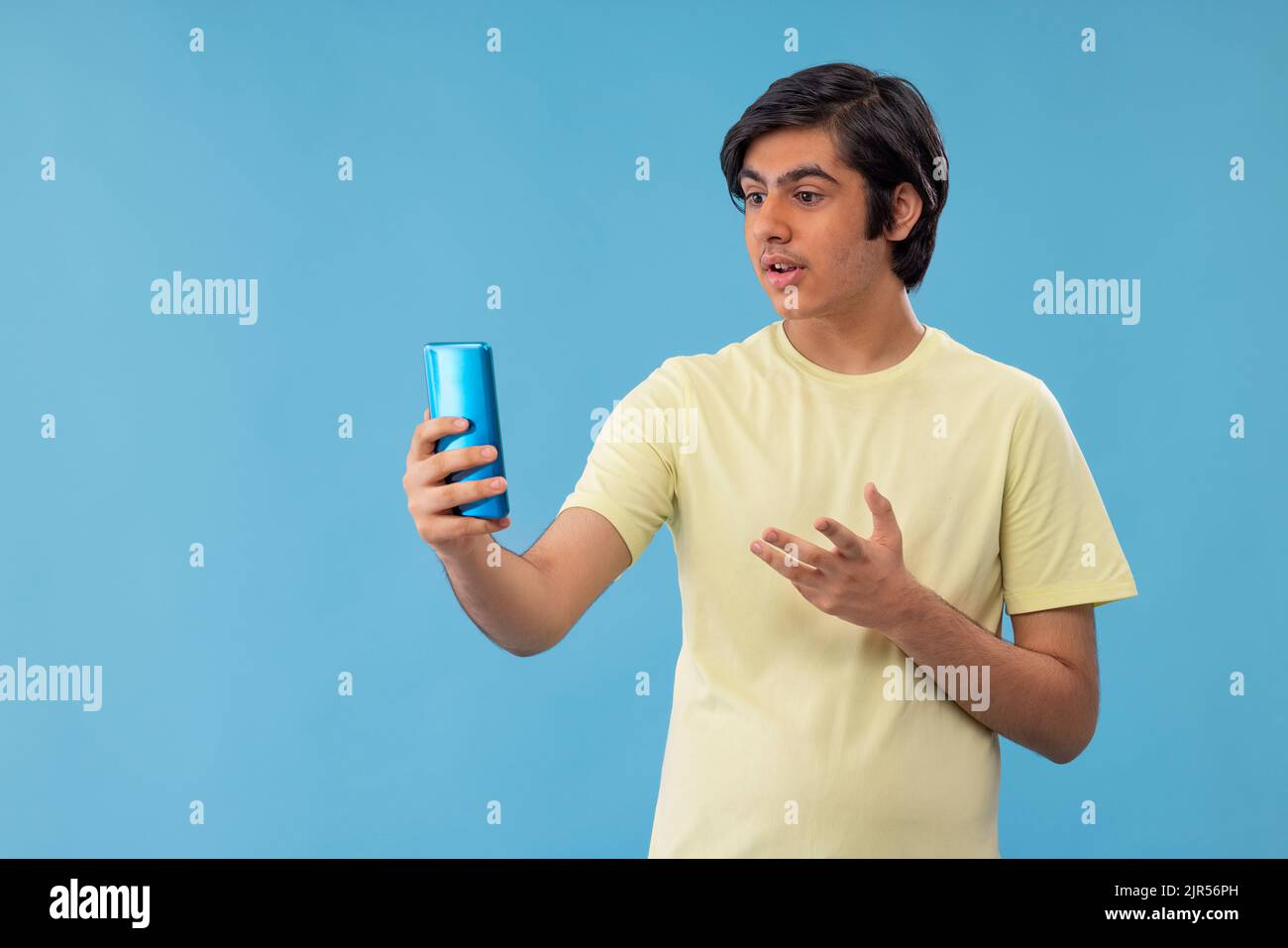 Teenage boy having video call on Smartphone against blue background ...