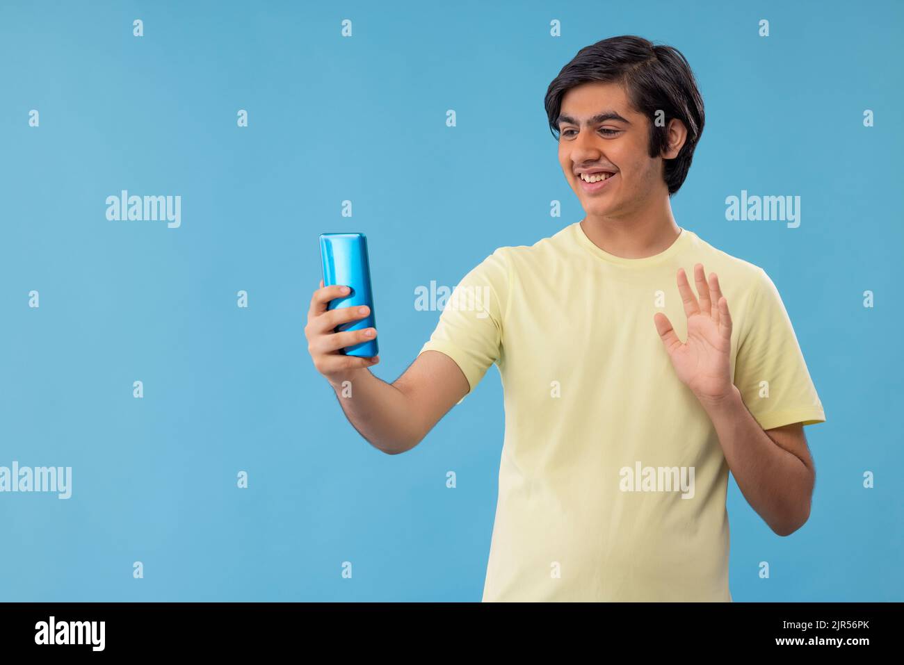 Teenage boy waving hand during video call on Smartphone against blue ...