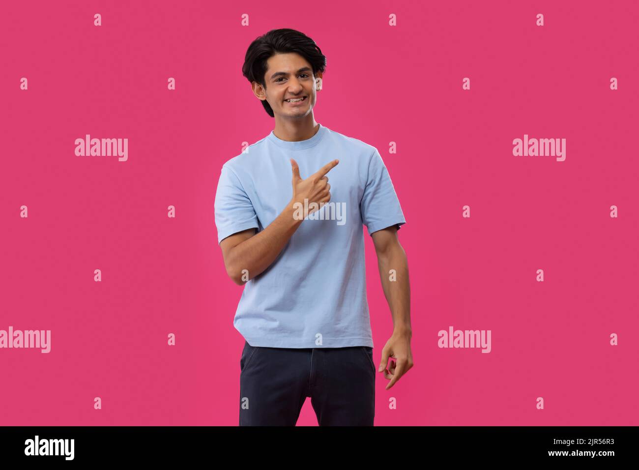 Portrait of a teenage boy making hand gesture against pink background ...