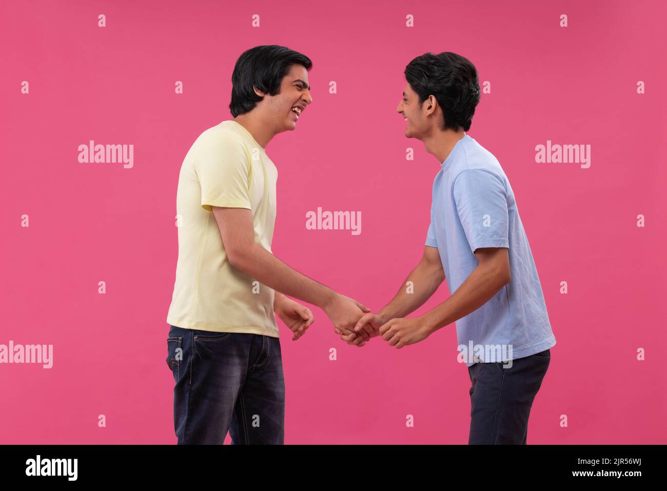 Portrait of two happy friends shaking hands against pink background ...