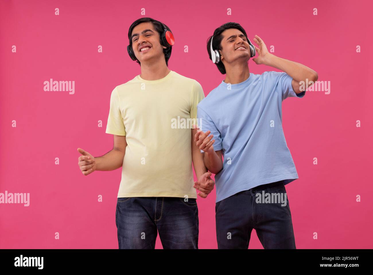 Two happy friends listening to music against pink background Stock ...