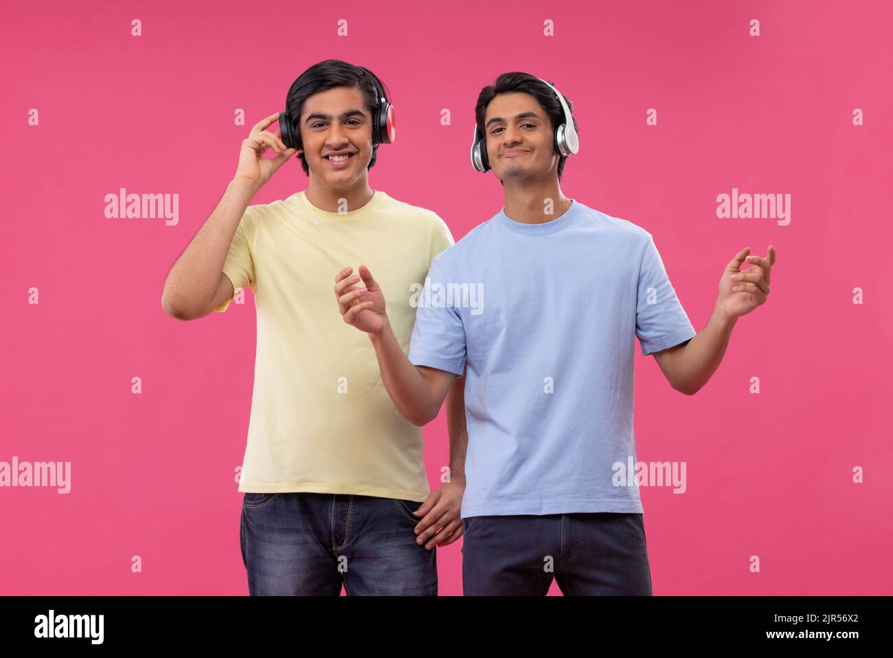 Two happy friends listening to music against pink background Stock ...