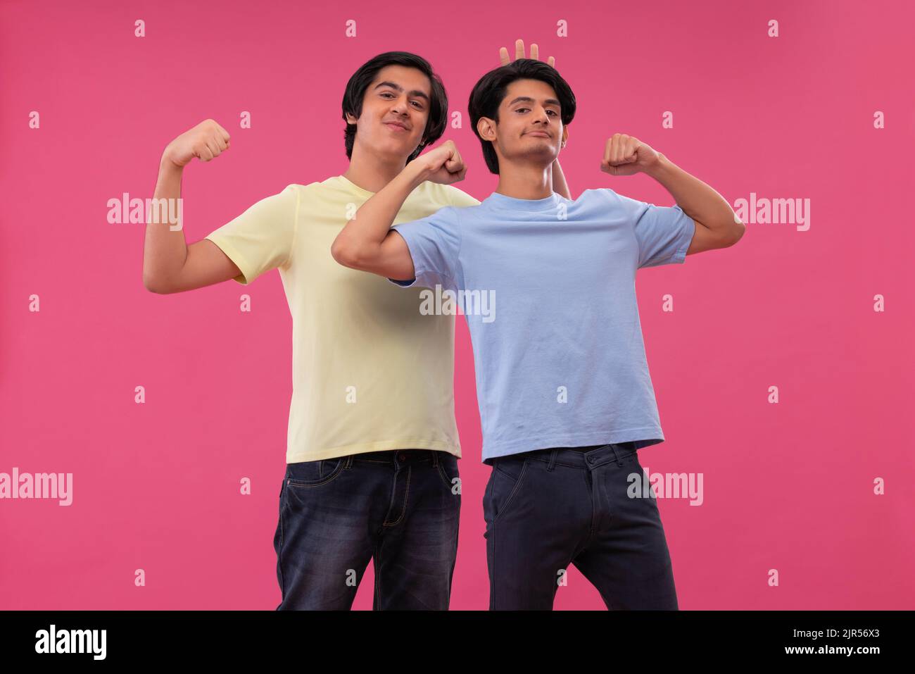 Portrait of two friends flexing muscles together against pink ...