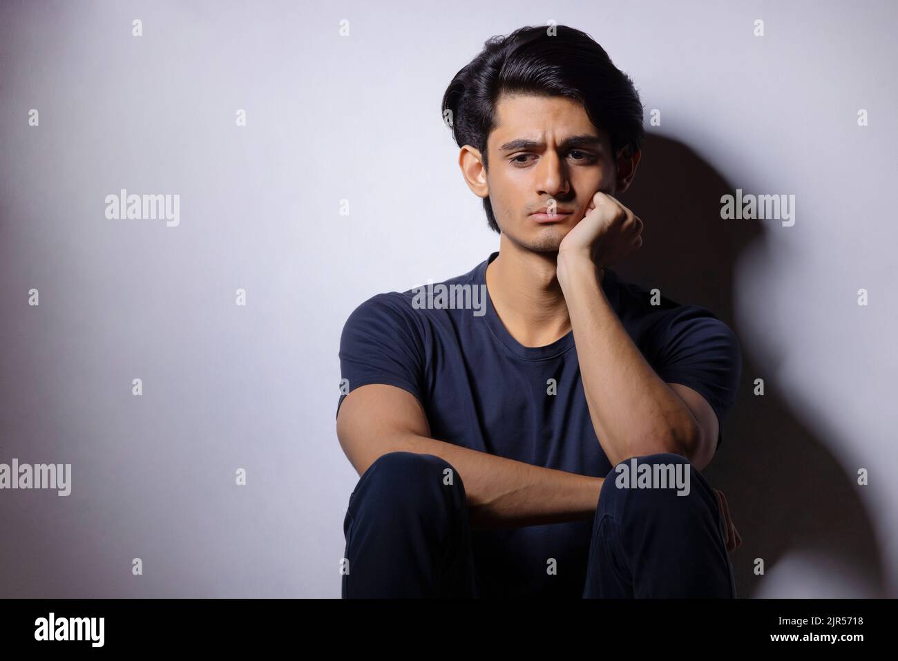 Portrait of a sad teenage boy with hand on chin sitting lonely at home ...