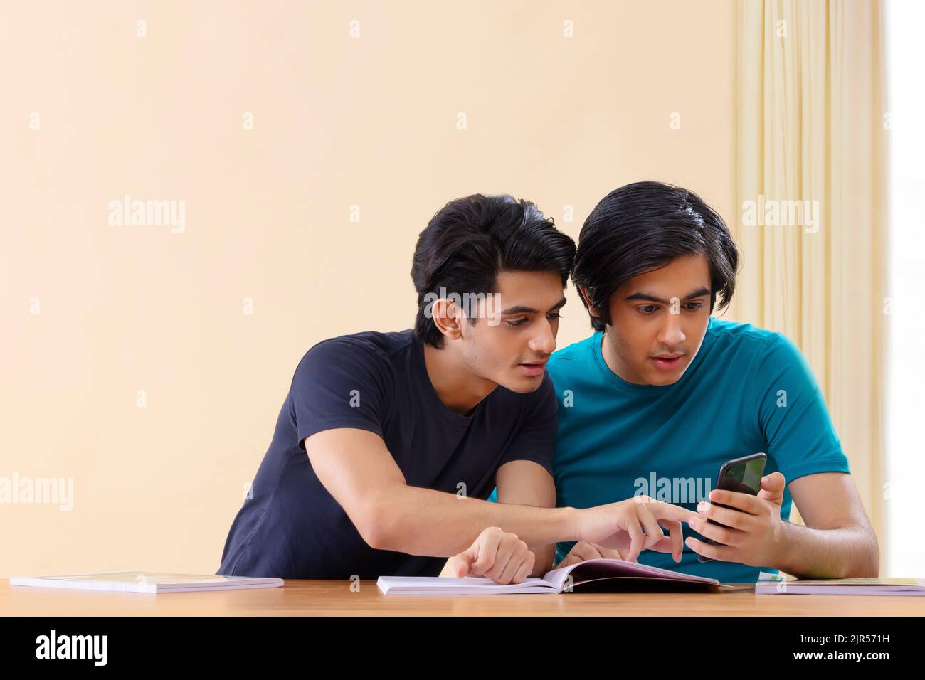 Two teenage boys using smartphone while studying together at home Stock ...