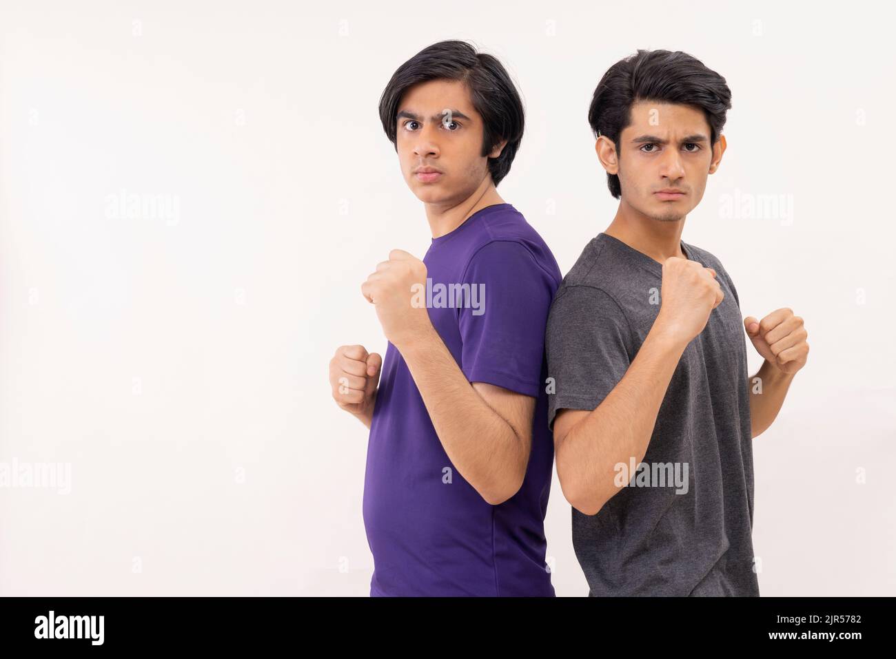 Portrait of two teenage boys standing back to back with their fists ...