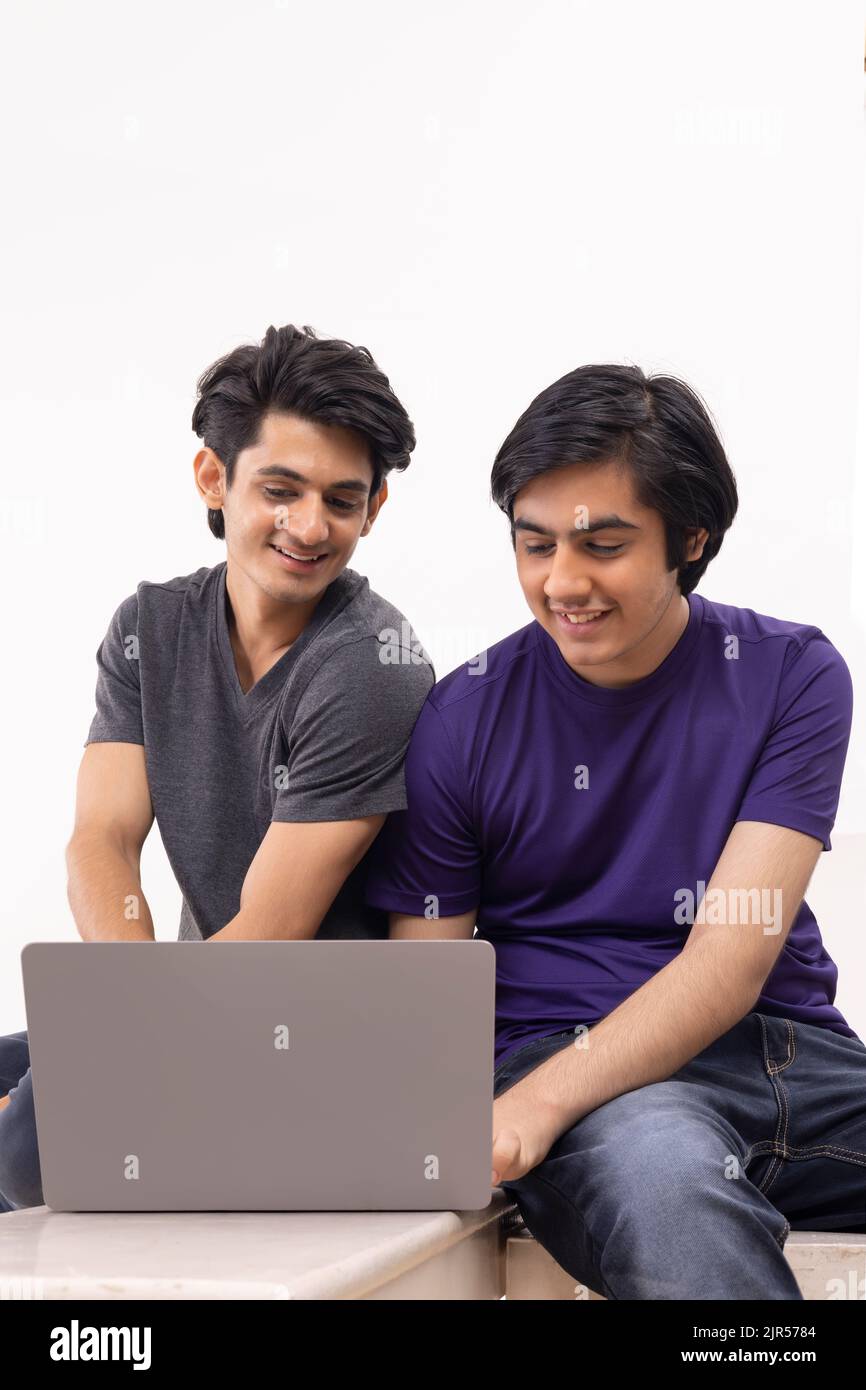 Portrait of two teenage boys using laptop against plain background ...