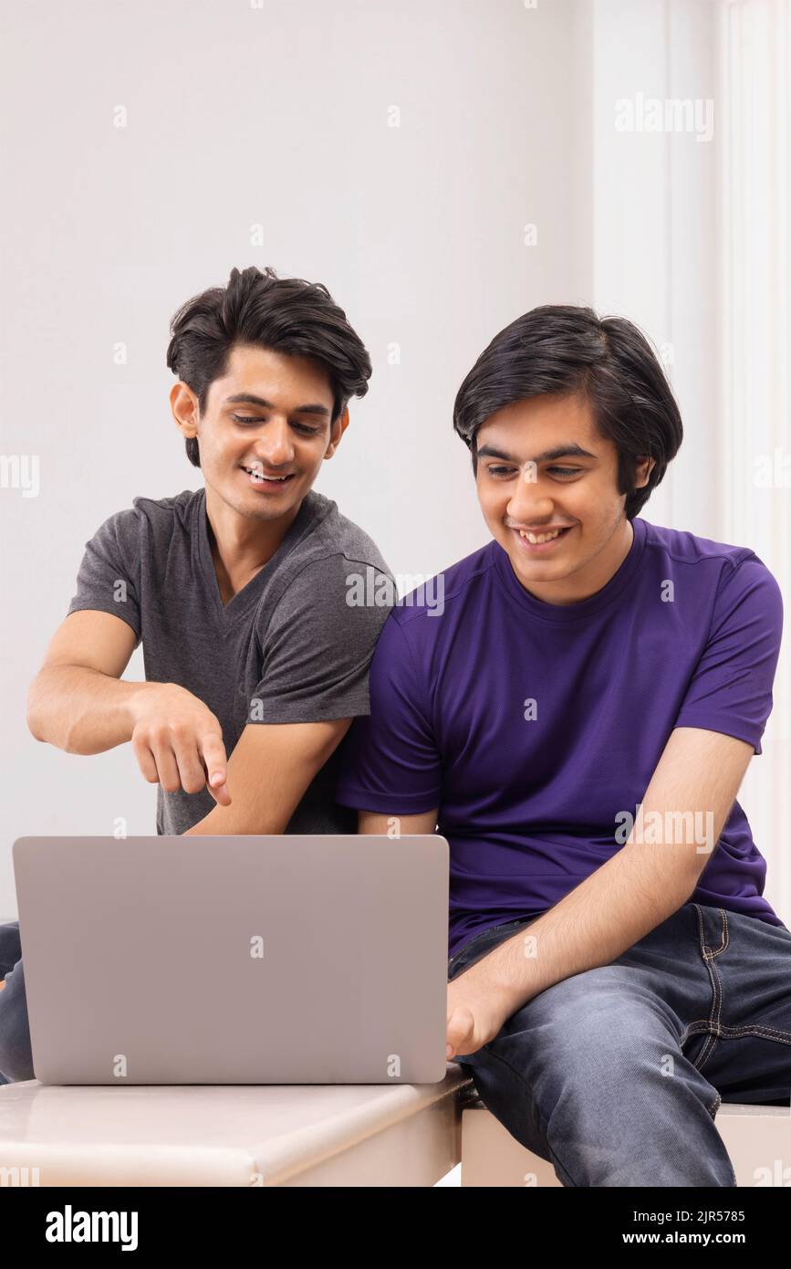 Portrait of two teenage boys using laptop against plain background ...