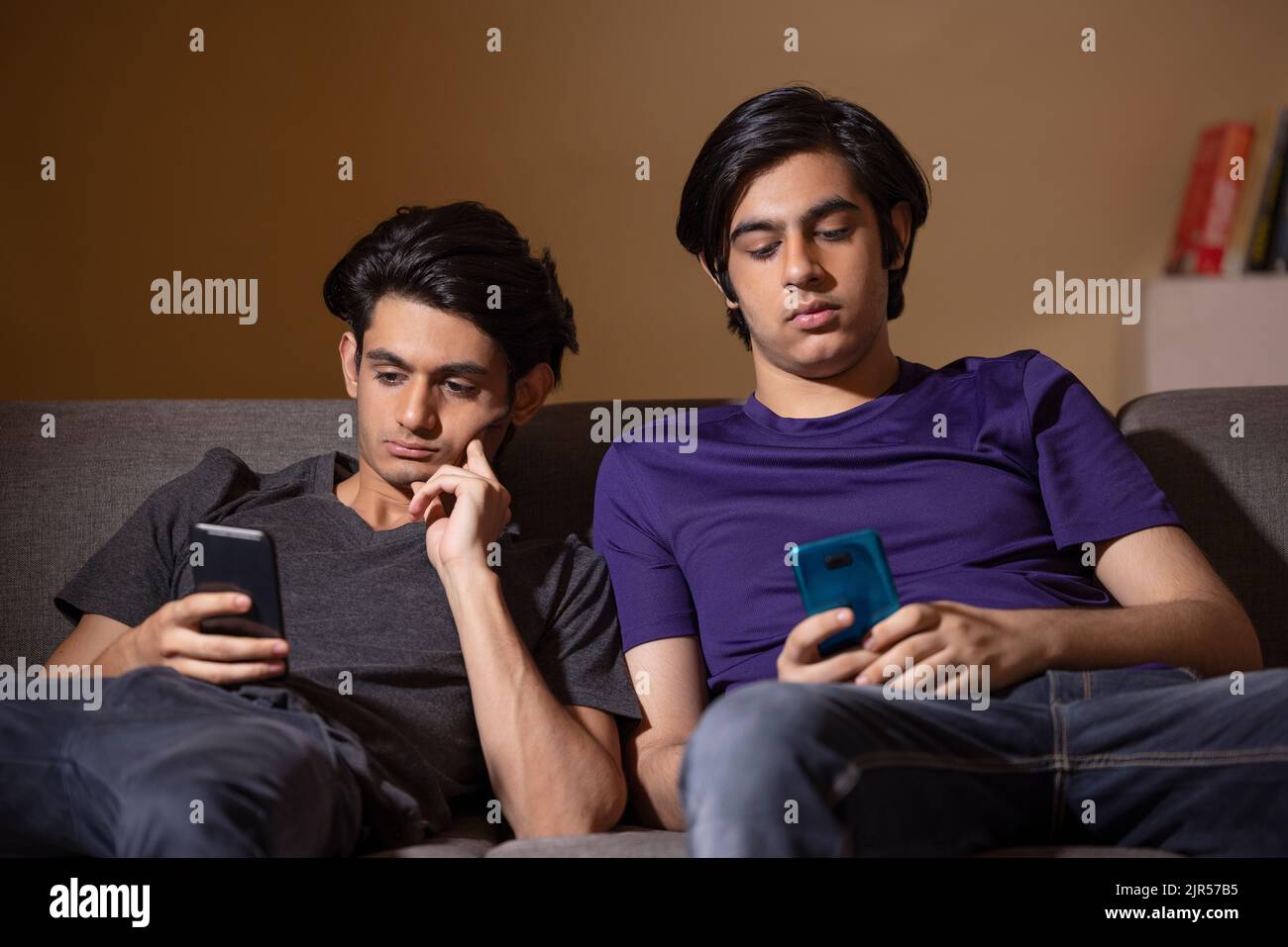 Portrait of two teenagers using smartphones while leaning on sofa in ...