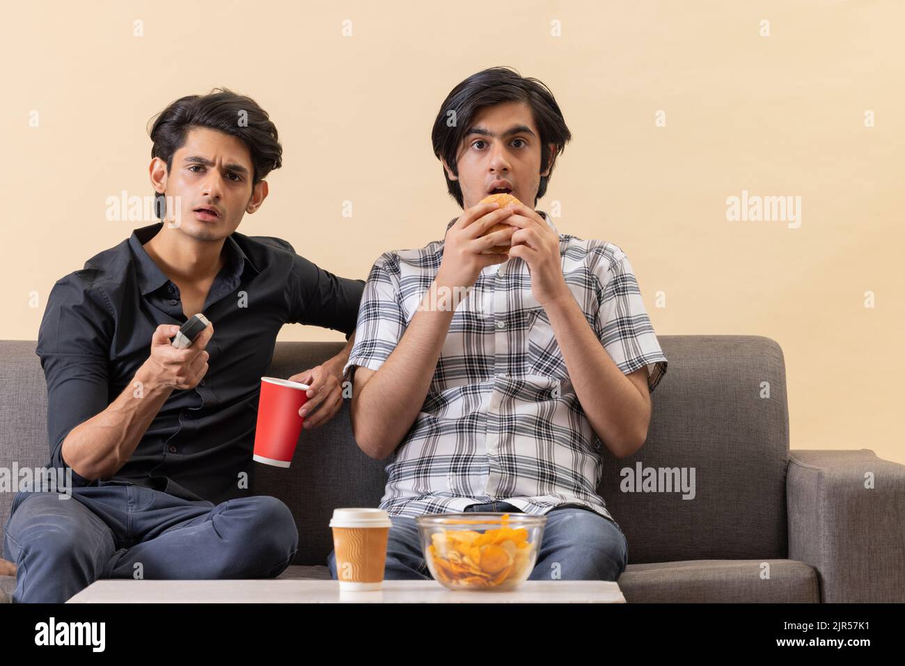 Two happy teenage boys eating fast foods and watching TV together at ...