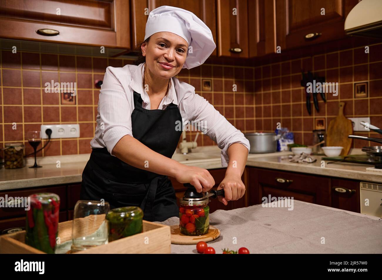 Pretty woman chef in white cap smiles at camera, using seamer closes ...