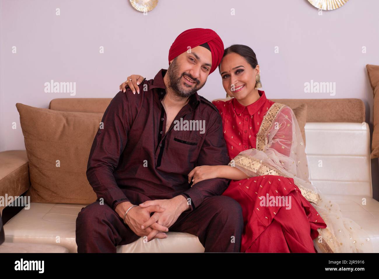 Portrait of a happy Sikh couple sitting together on sofa in living room ...