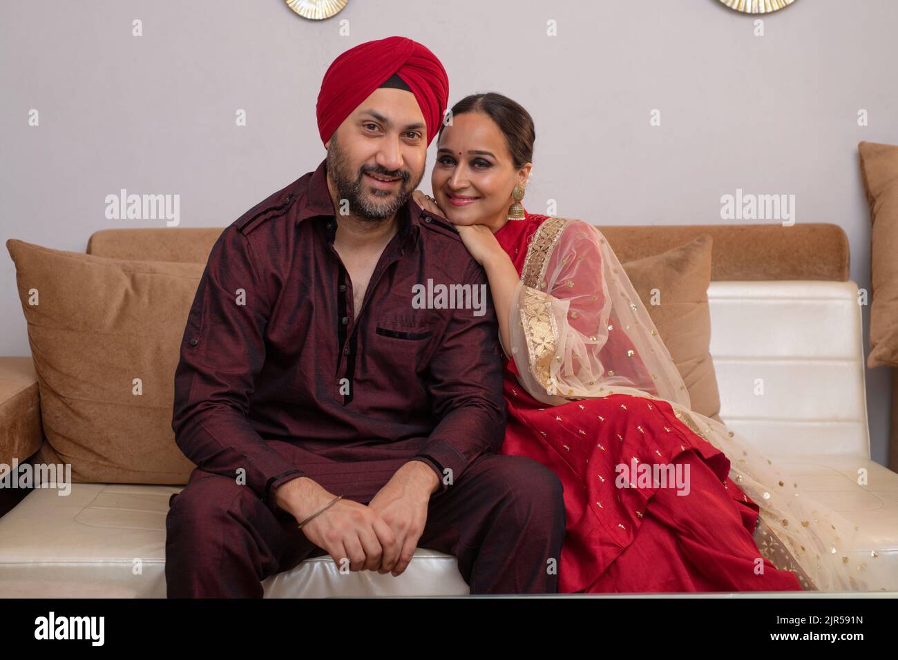 Portrait of a happy Sikh couple sitting together on sofa in living room ...