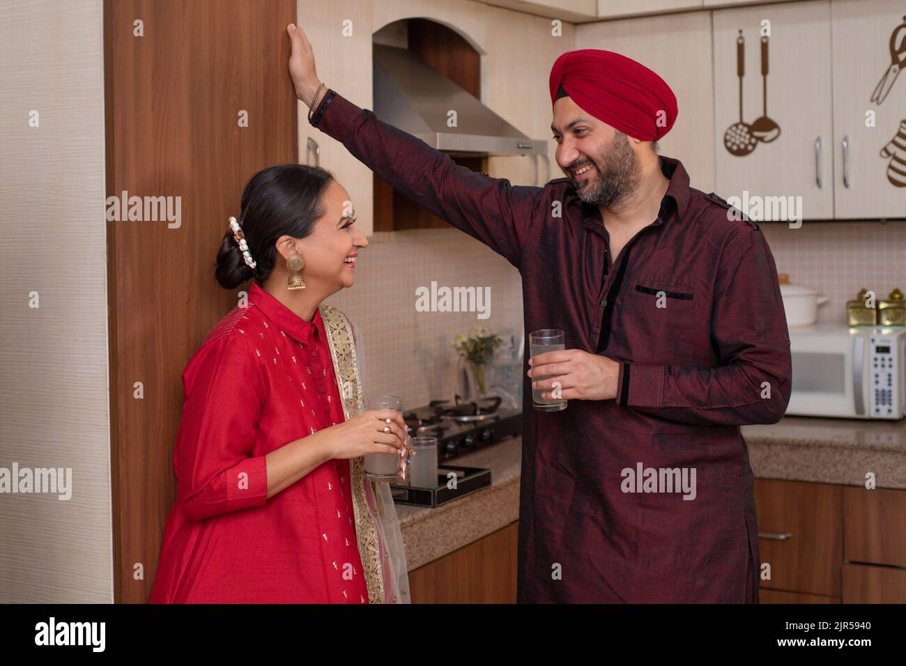 Happy Sikh couple standing in the kitchen with glass of drink Stock ...