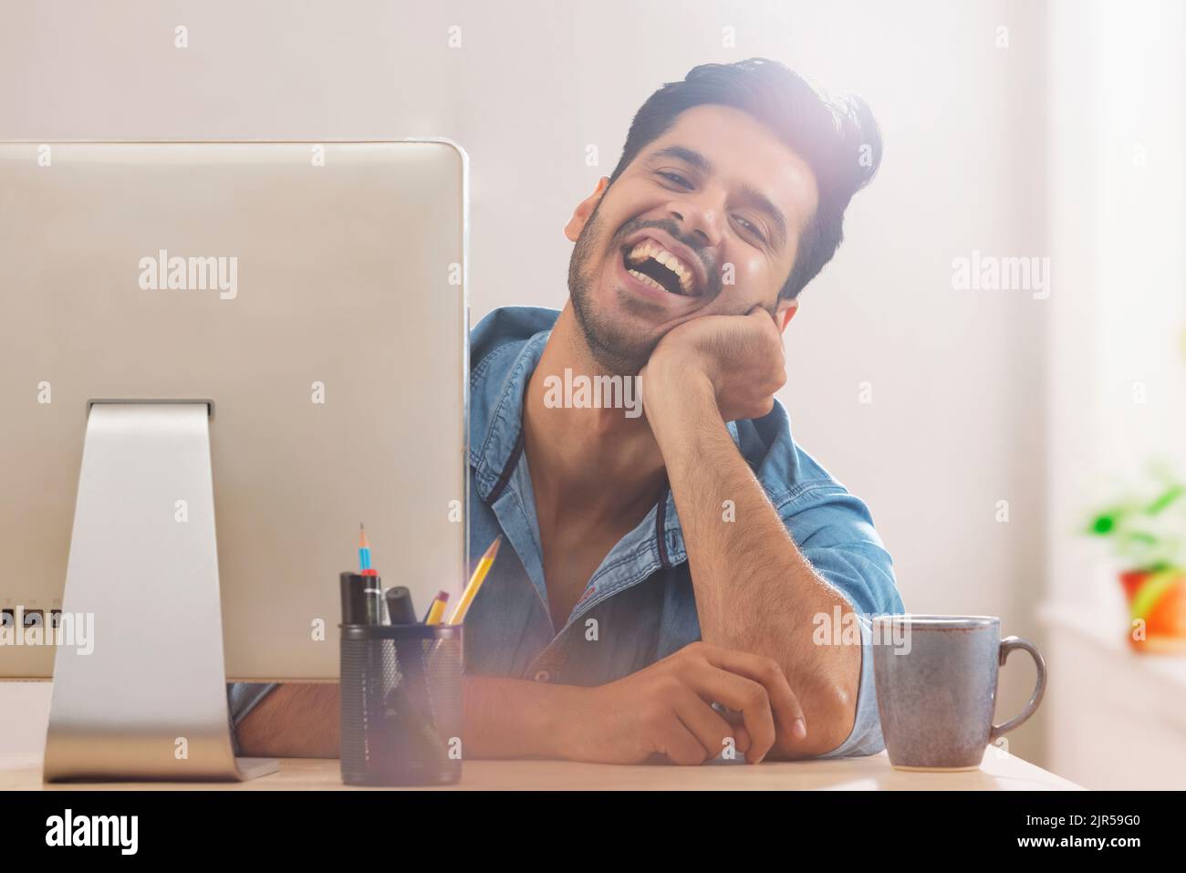 A corporate employee in formal clothing smiling behind his desktop at ...