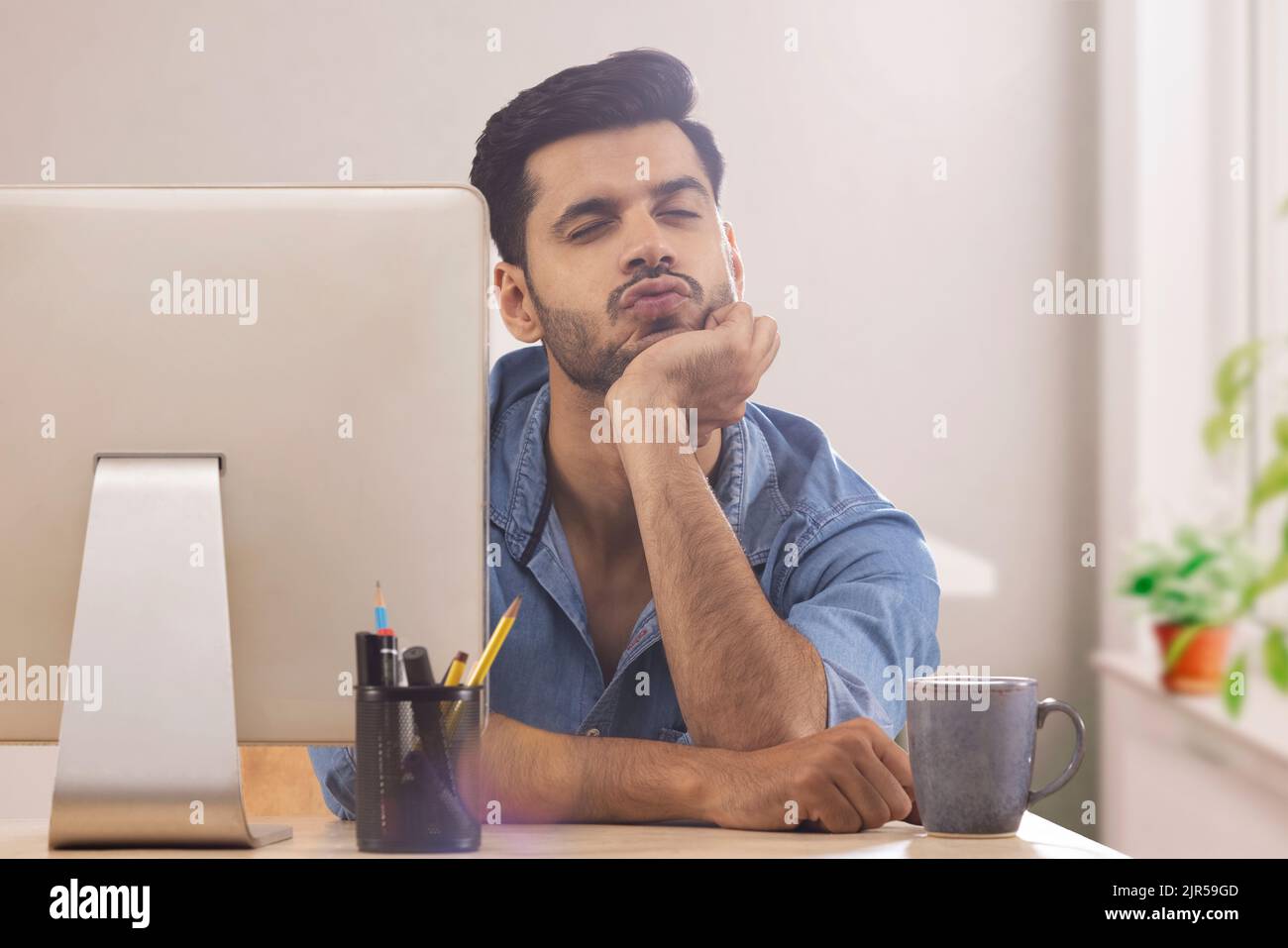A corporate employee in formal clothing pouting behind his desktop at ...