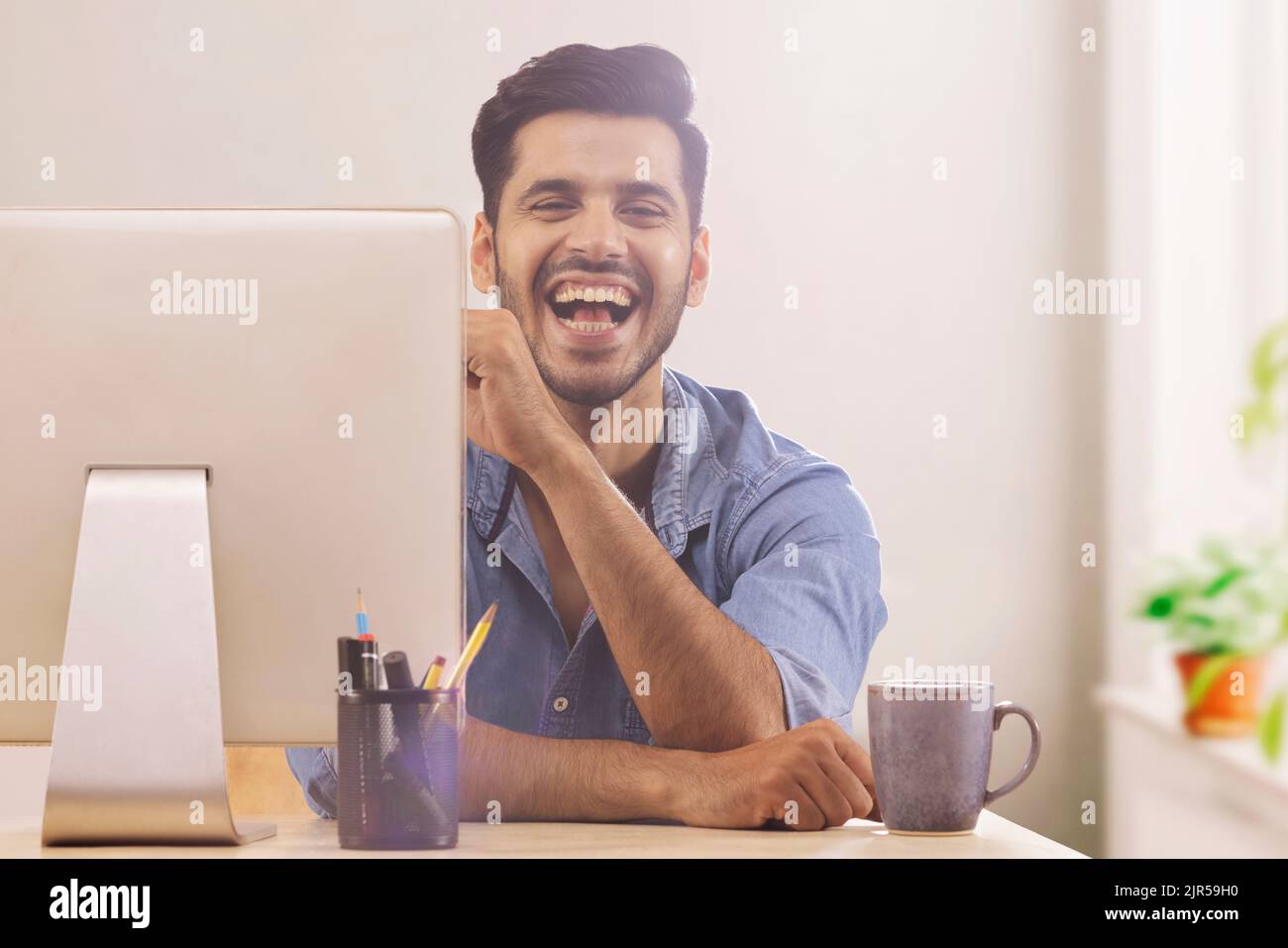 A corporate employee in formal clothing smiling behind his desktop at ...