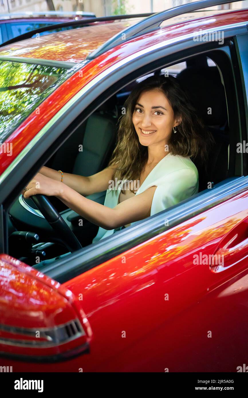 Happy smiling woman driver behind the wheel red car. View through car ...