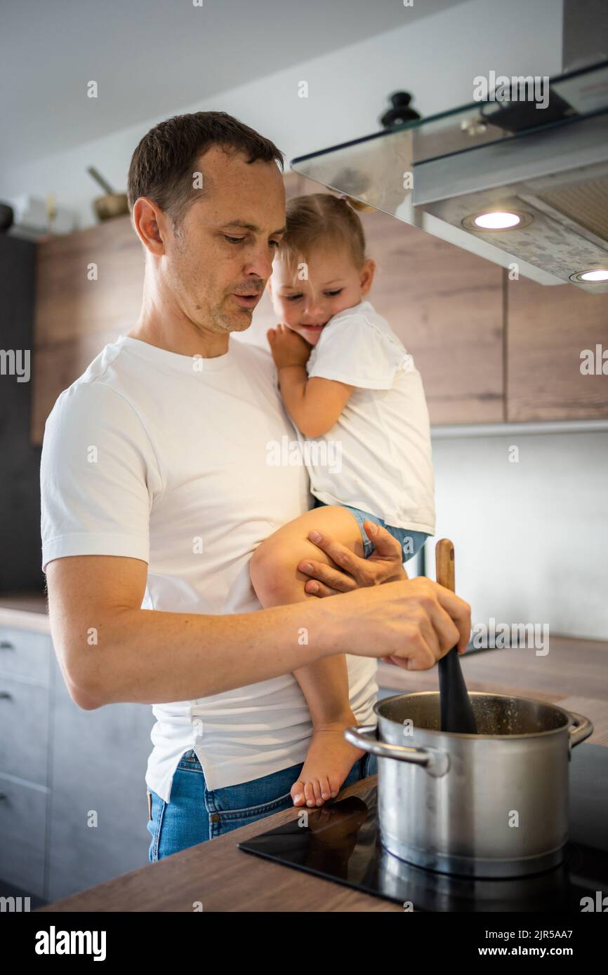 Father with his daughter on his hands cooking soup together in modern ...
